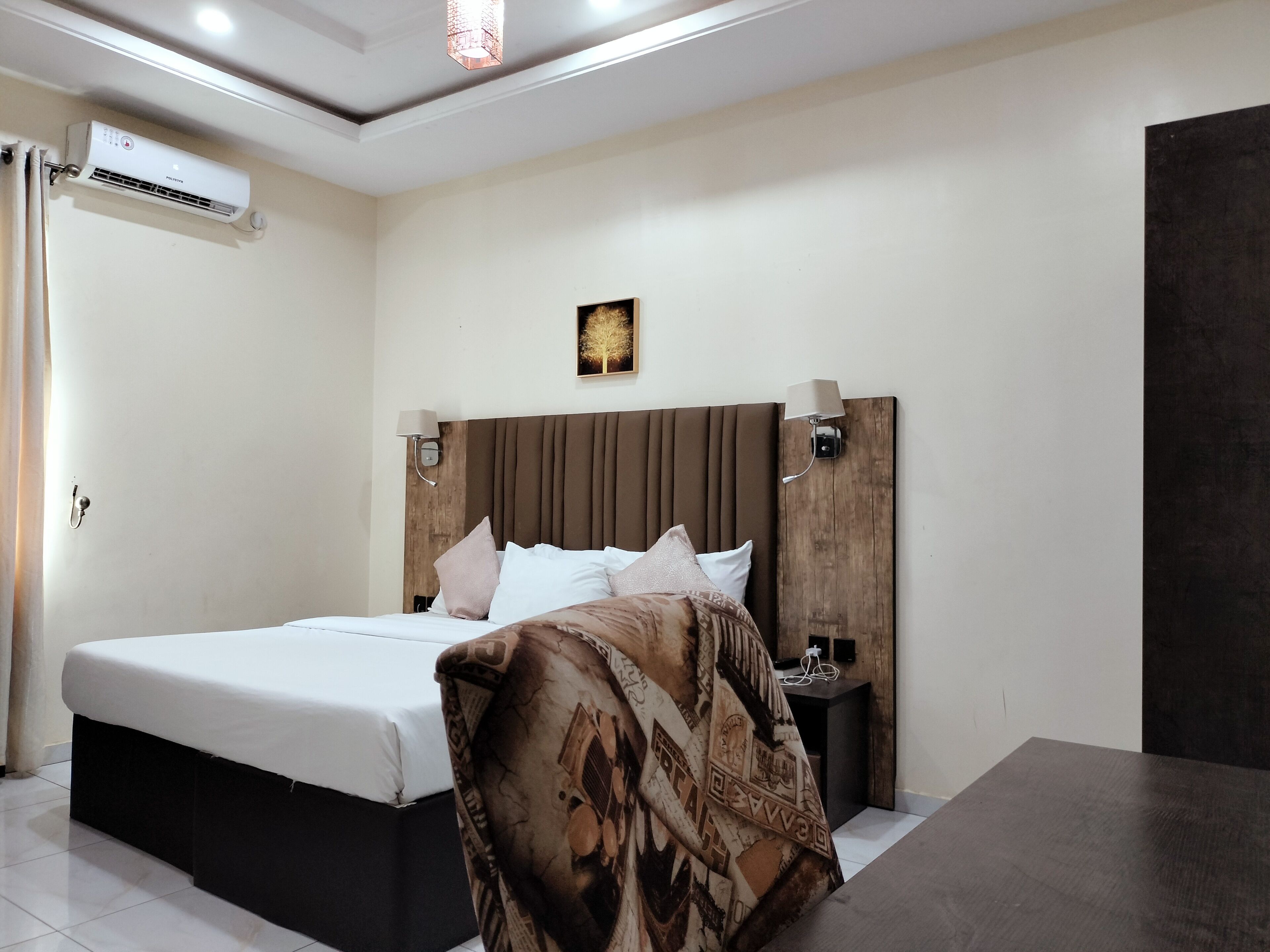 Quarto de hotel com cama, mesas de cabeceira, ar condicionado e luminária na parede.