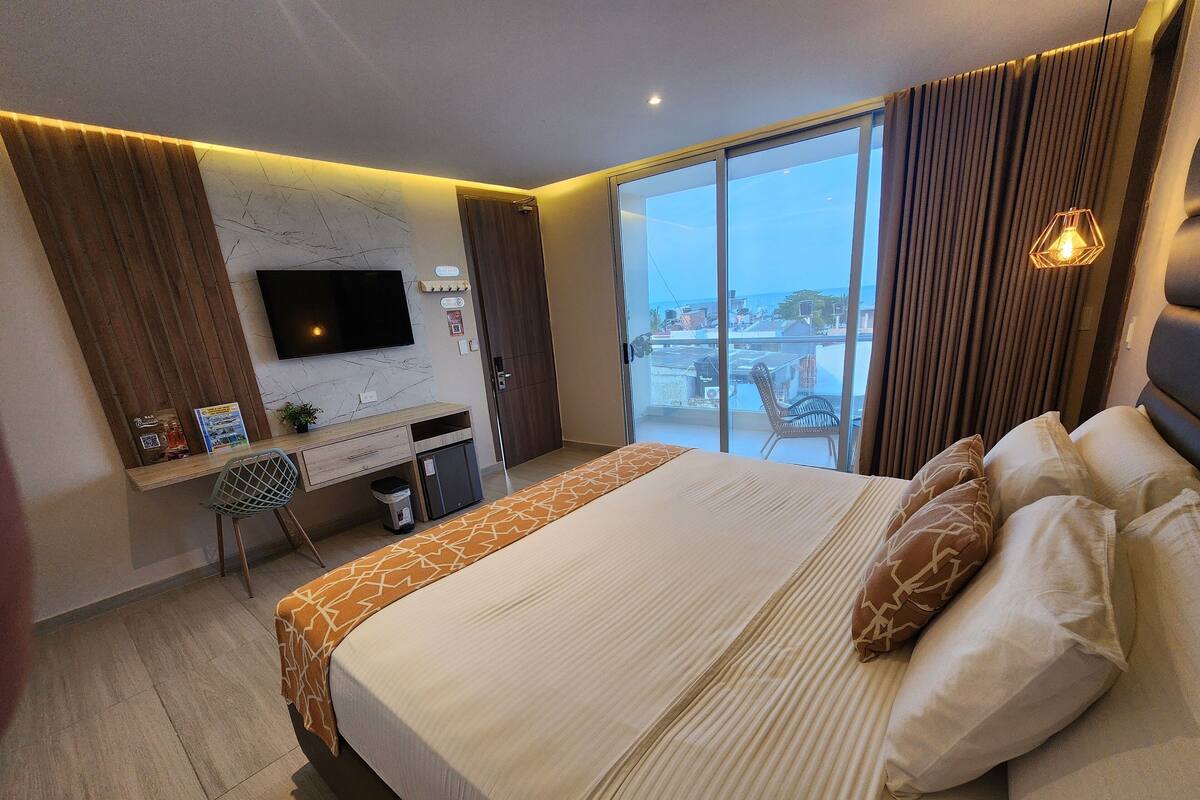 Quarto de hotel moderno com uma cama grande, uma escrivaninha com televisão de tela plana e uma varanda com vista.