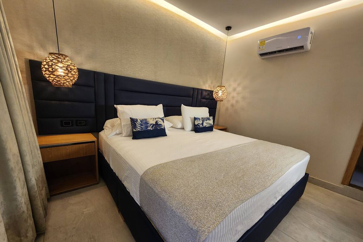 Quarto moderno com uma cama grande, duas mesas de cabeceira e ar condicionado fixado na parede.