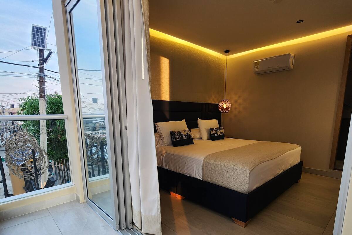 Quarto moderno com uma cama grande, uma porta de vidro deslizante que dá para uma varanda e um aparelho de ar condicionado na parede.