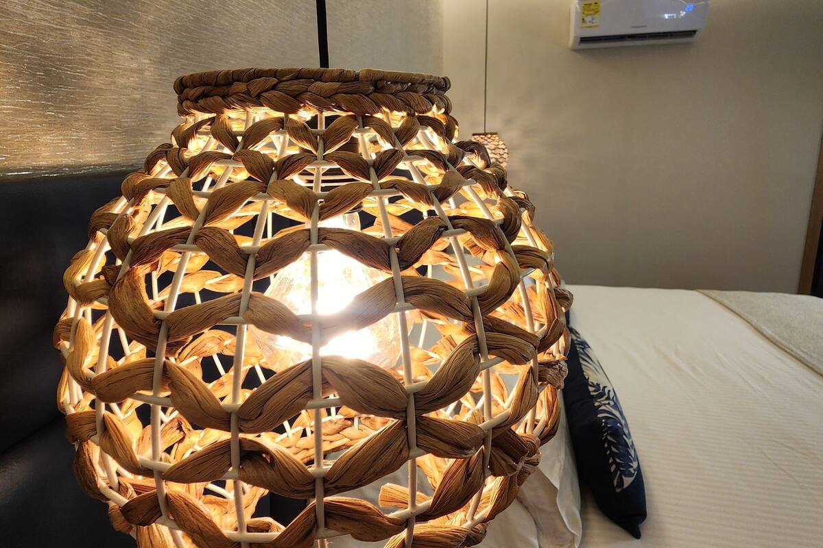 Quarto com luminária de fibra trançada, cama com travesseiro e ar condicionado na parede.
