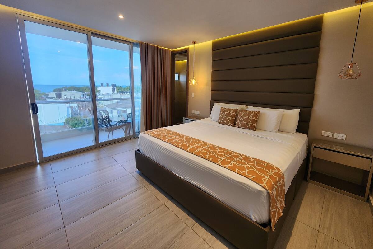 Quarto de hotel moderno com uma cama grande, vista da cidade e varanda.