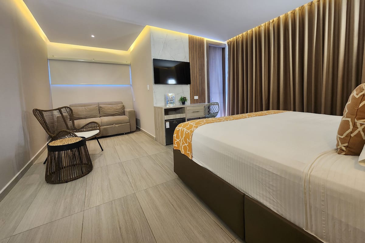 Quarto de hotel moderno com uma cama grande, um sofá, uma mesa de escritório com televisão e um espaço de refeições.