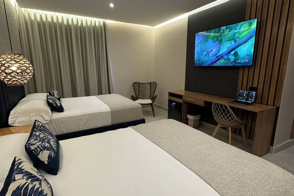 Quarto de hotel moderno com uma cama grande, uma escrivaninha com um laptop, uma televisão e uma cadeira.