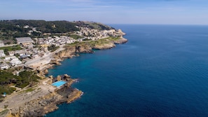 Uma cidade costeira com edifícios ao longo da orla, um litoral rochoso e uma vista clara do mar.