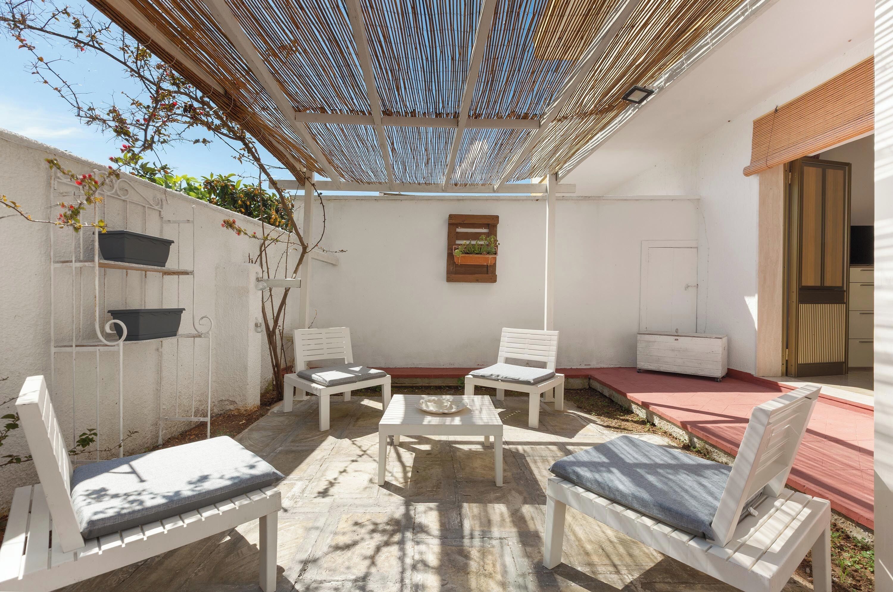 Área de pátio com móveis brancos, uma mesa e um vaso pendente.