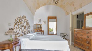 Quarto com cama, penteadeira, escrivaninha com luminária e espelho.
