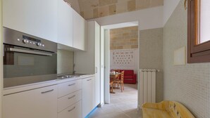 Cozinha com armários brancos, forno de aço inoxidável e área de refeições com sofá vermelho e mesa.
