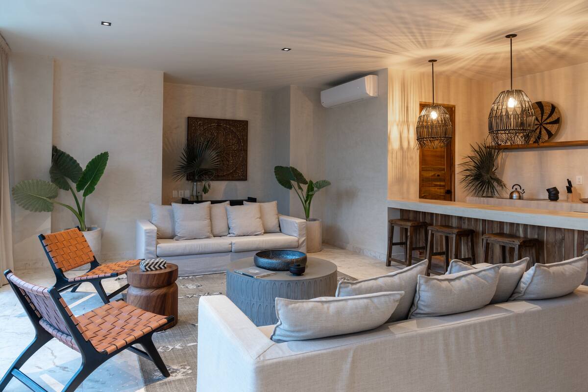 Uma sala de estar moderna com sofá, cadeiras, mesa de centro e um espaço bar com banquetas.