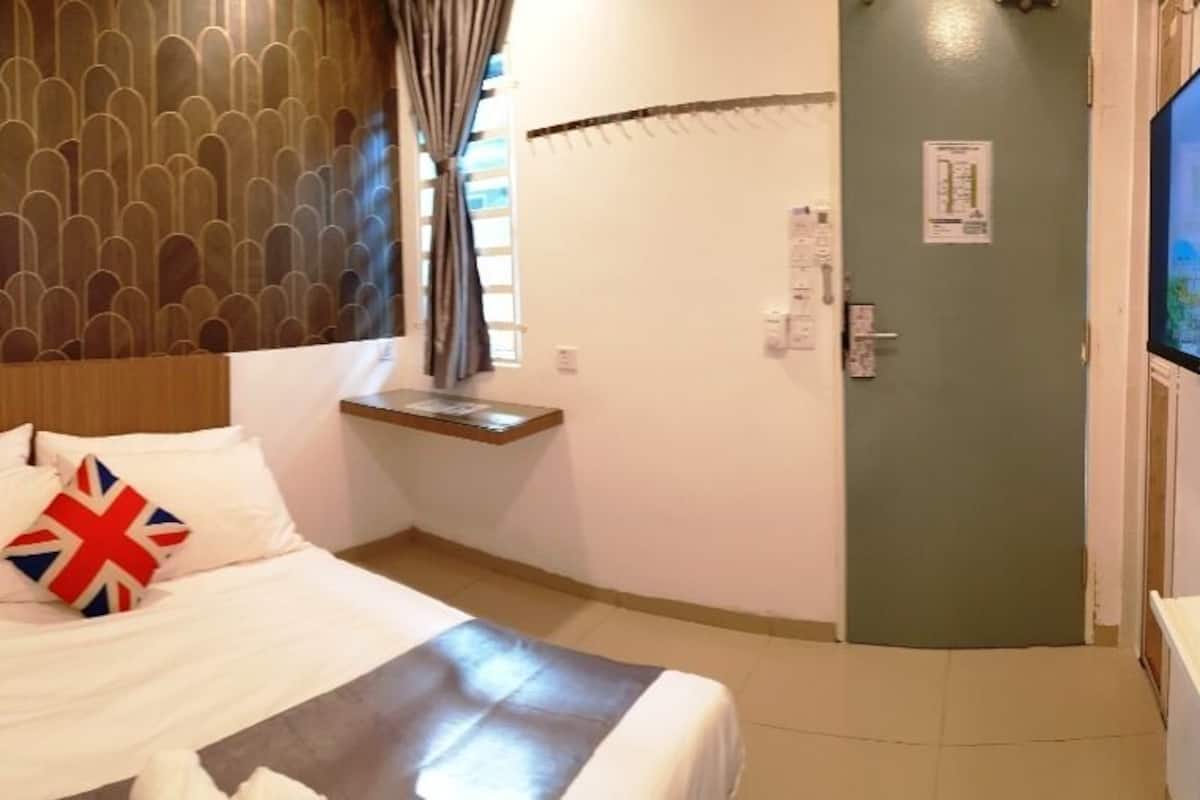 Quarto de hotel com uma cama, uma mesa pequena, uma televisão e uma cortina.
