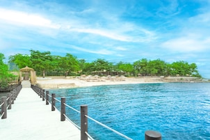 Um píer que dá para uma praia com guarda-sóis e espreguiçadeiras.