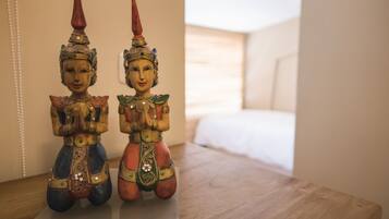 Duas figuras de madeira ornamentadas sobre um suporte de vidro transparente em um quarto com uma cama ao fundo.