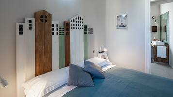 Quarto com cama, almofadas, mesa de cabeceira, luminária na parede e um quadro emoldurado.