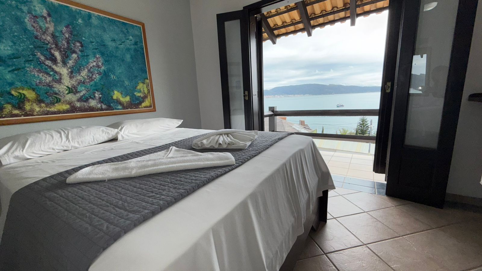 Quarto de hotel com cama, um quadro e vista para o mar por uma porta aberta.