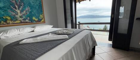 Quarto de hotel com cama, um quadro e vista para o mar por uma porta aberta.