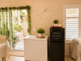 Quarto com um relógio na parede, uma geladeira com uma mensagem de boas-vindas e vista para um jardim através de uma porta de vidro.