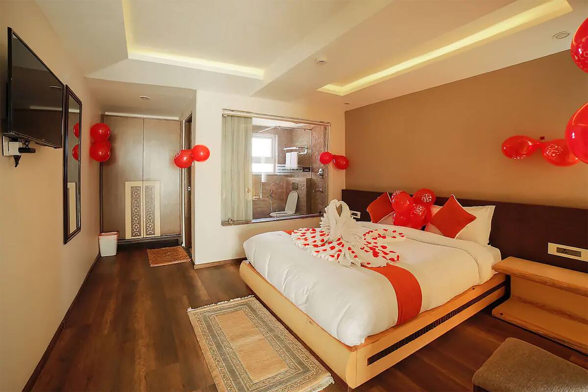 Quarto moderno com cama de madeira, um espelho grande e balões vermelhos.