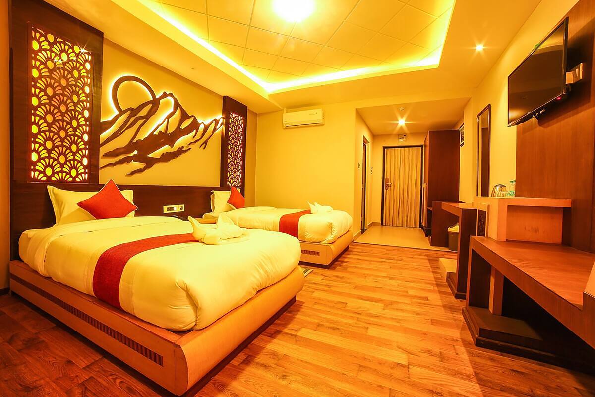 Quarto de hotel com uma cama grande, uma cama menor, uma escrivaninha e uma televisão.