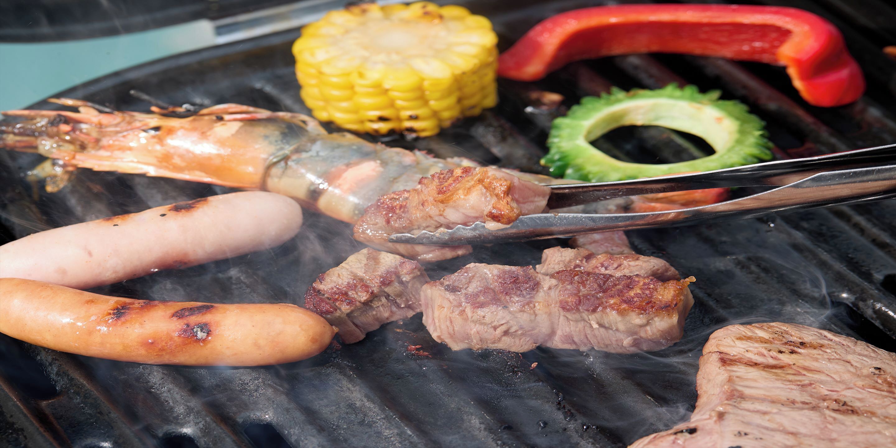 Uma churrasqueira com diversos tipos de carne e legumes sendo preparados.