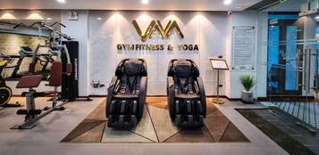 Ginásio com duas cadeiras de massagem, equipamentos de exercício e uma parede de mármore com o nome do ginásio.