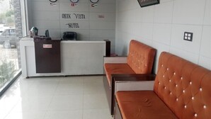 Uma área de recepção de hotel, com balcão de atendimento, sala de espera com sofá e relógios exibindo diferentes fusos horários.