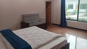 Quarto com cama, sofá de encosto estofado, janela com cortinas e vista para o exterior.