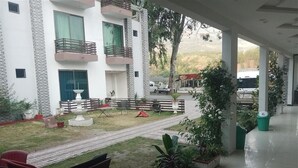 Área externa coberta com calçada pavimentada, plantas em vasos e assentos ao ar livre.
