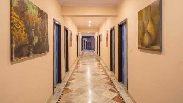 Um corredor de hotel com piso de mármore, portas azuis e obras de arte nas paredes.
