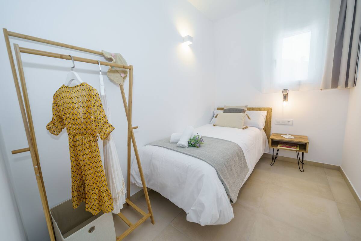 Quarto com cama, guarda-roupa de madeira, mesa de cabeceira e luminária na parede.