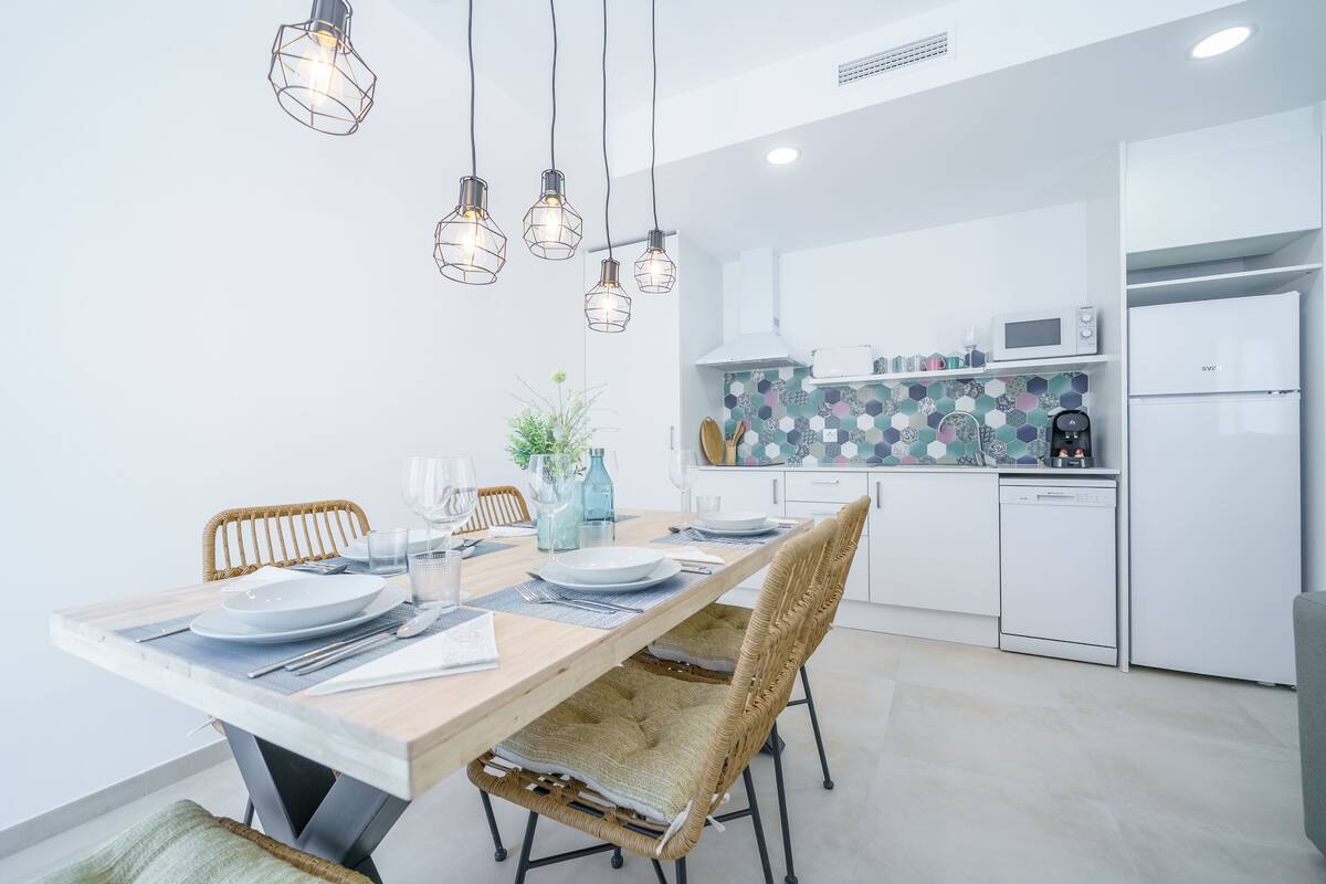 Cozinha moderna com armários brancos, micro-ondas e máquina de lavar louça. Há uma mesa de jantar com cadeiras e um vaso com flores.