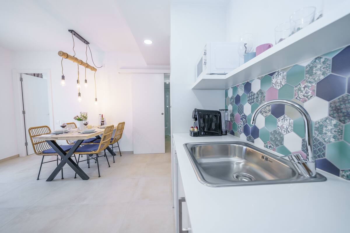 Uma cozinha moderna com uma pia de aço inoxidável, uma área de refeições com mesa e cadeiras de madeira, e um lustre.
