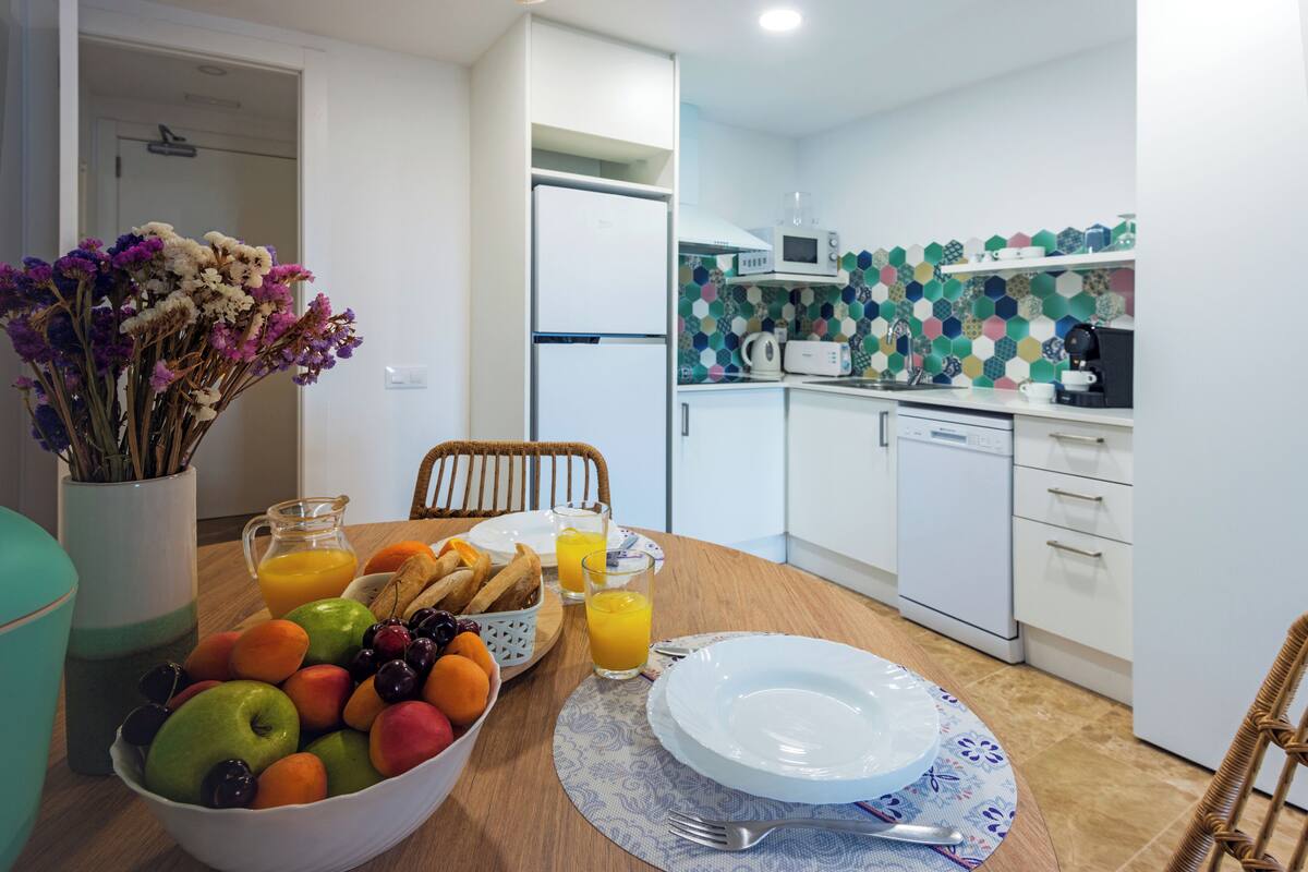 Uma mesa de jantar com frutas, um jarro de suco e um vaso de flores.