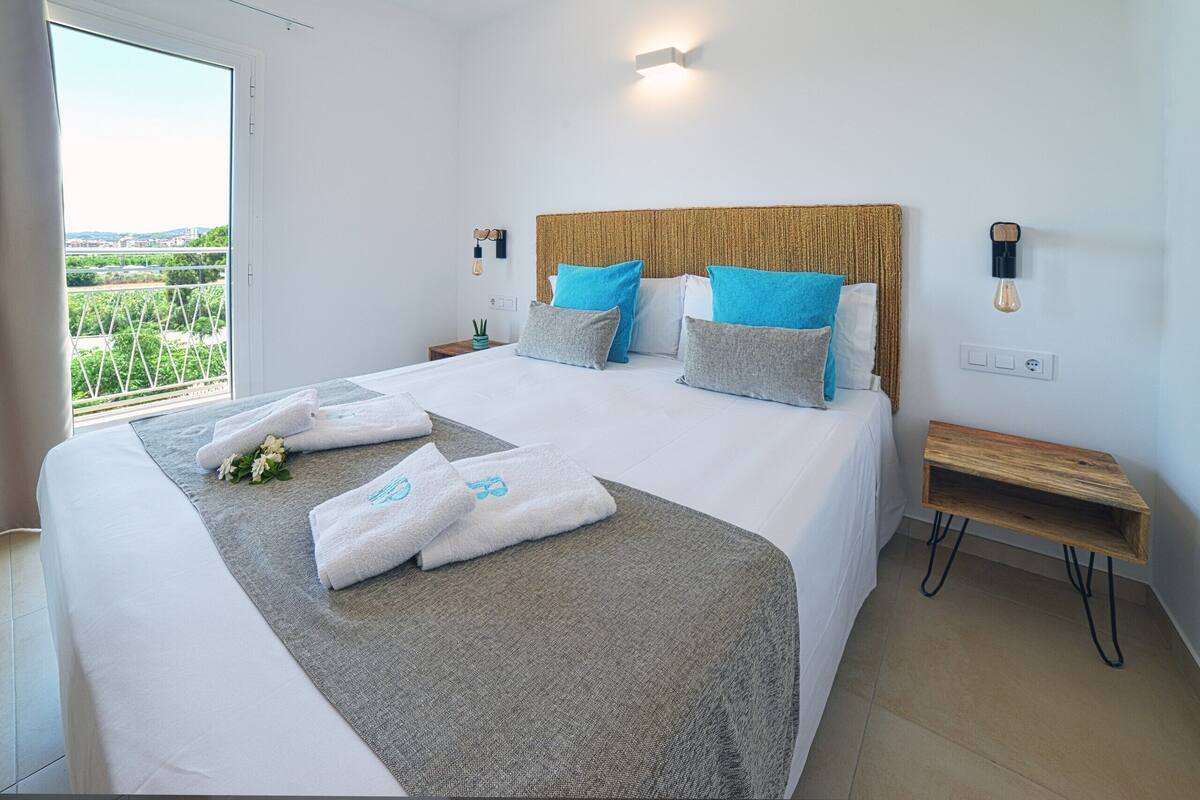 Cama bem arrumada com toalhas e vista para o verde lá fora.