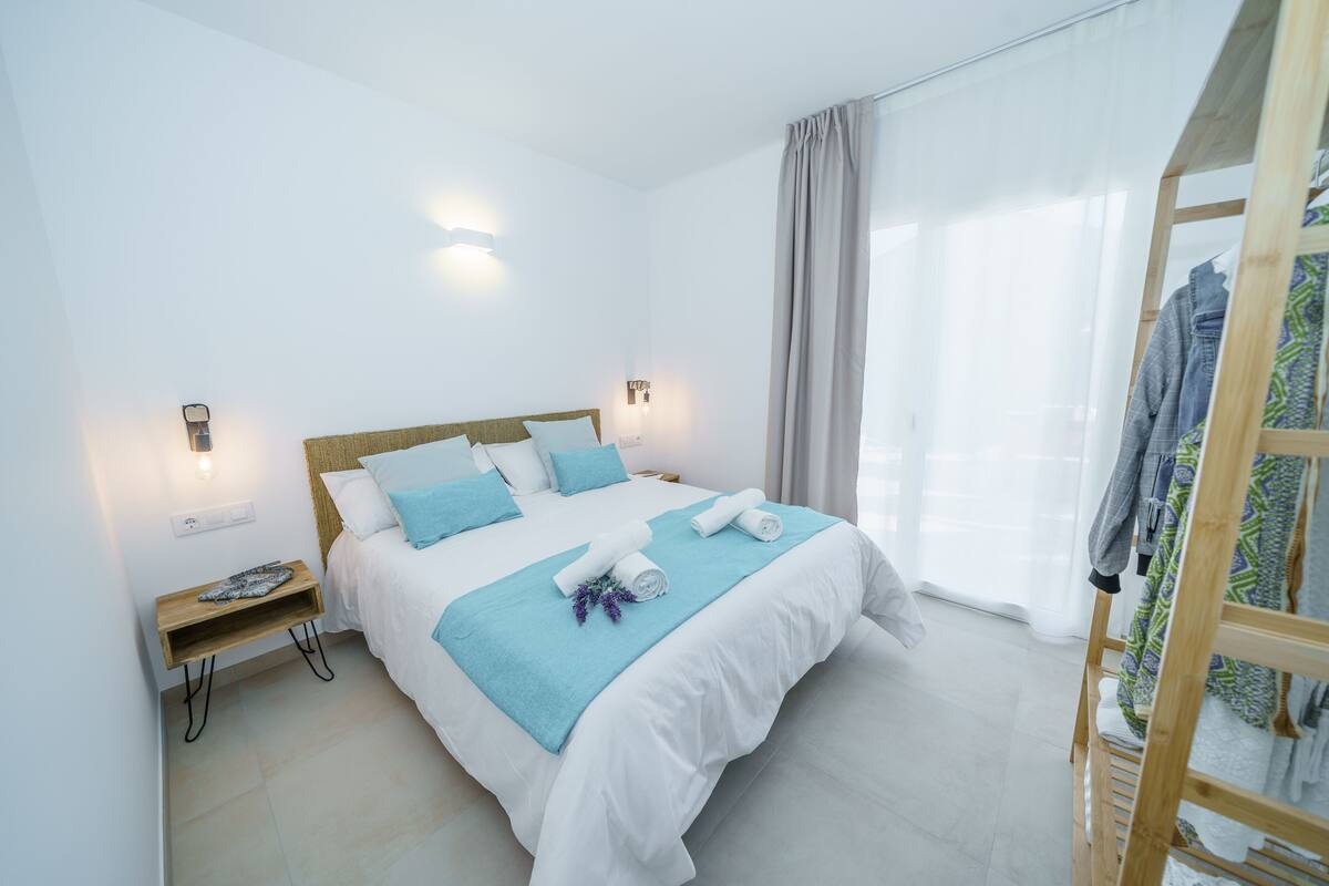 Quarto de hotel moderno com uma cama grande, uma mesinha de cabeceira de madeira e um guarda-roupa de madeira.
