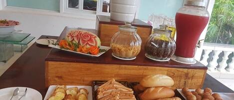 Um buffet de café da manhã com pães, doces e uma seleção de frutas.