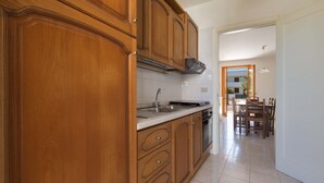 Cozinha com armários de madeira, pia de aço inoxidável e área de jantar com mesa e cadeiras.