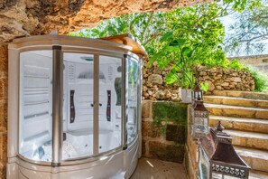 Uma área de spa com chuveiro em compartimento de vidro, paredes de pedra e um pequeno candeeiro.