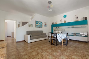 Uma sala de estar acolhedora, com um sofá, uma mesa de jantar com cadeiras e uma área de cozinha com prateleiras.