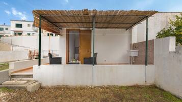 Um pátio moderno ao ar livre com pérgola de madeira, área de estar com mesa e cadeiras, e vista para um edifício residencial ao fundo.
