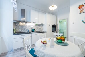 Cozinha moderna com armários brancos, painel de azulejos e uma área de jantar com mesa posta para dois.