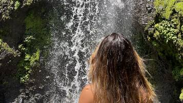 Uma pessoa em frente a uma cachoeira, com água caindo sobre uma superfície rochosa.
