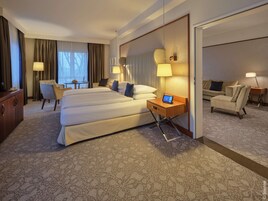 Quarto de hotel com uma cama grande, duas mesas de cabeceira, uma escrivaninha, uma cadeira e um sofá.