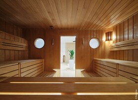 Uma sauna com bancos de madeira e uma passagem central, que leva a uma porta de vidro.