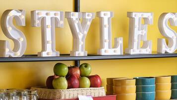 Estante com letras decorativas formando a palavra 'STYLES', uma cesta de vime com maçãs e xícaras de cerâmica empilhadas.
