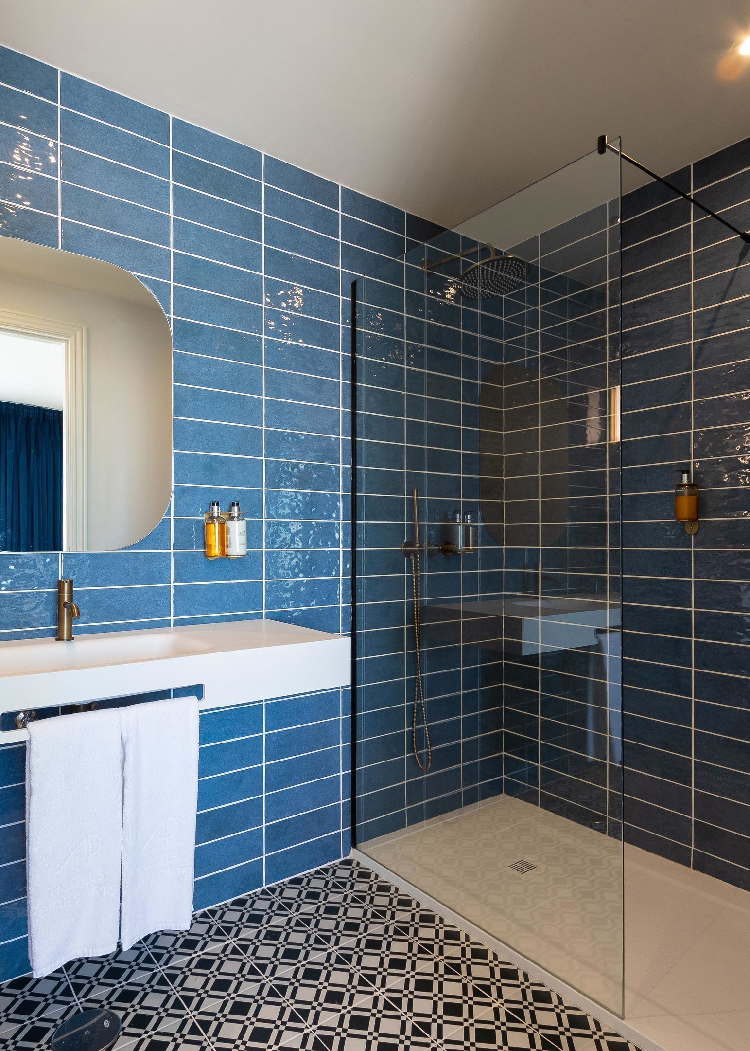 Uma casa de banho moderna com chuveiro em azulejo azul, lavatório branco e um espelho grande.