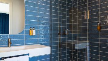Uma casa de banho moderna com chuveiro em azulejo azul, lavatório branco e um espelho grande.