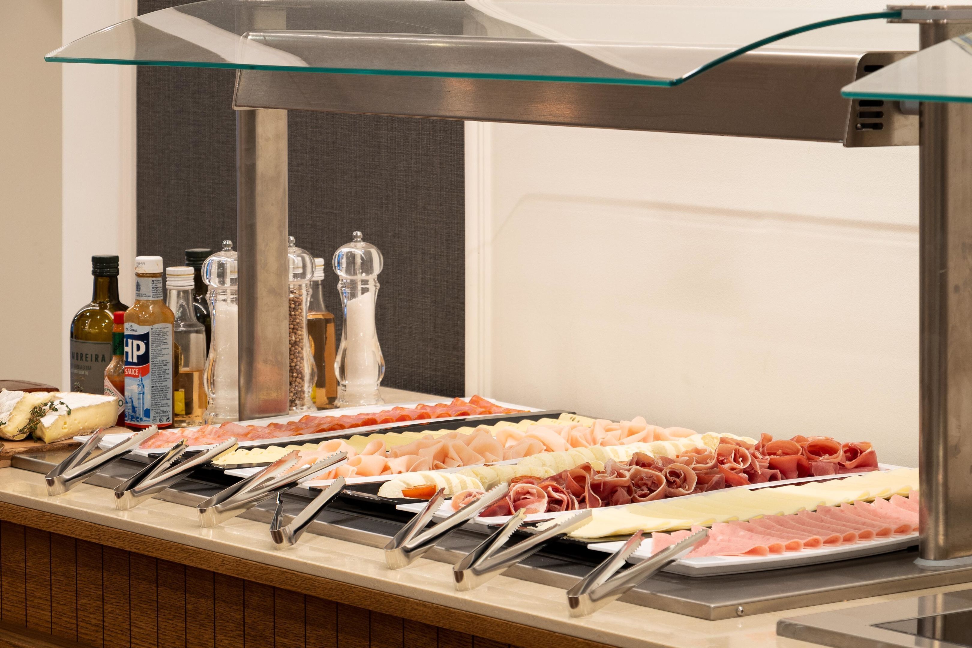 Buffet com diversos carnes e queijos, incluindo presunto, salame e diferentes tipos de queijo.