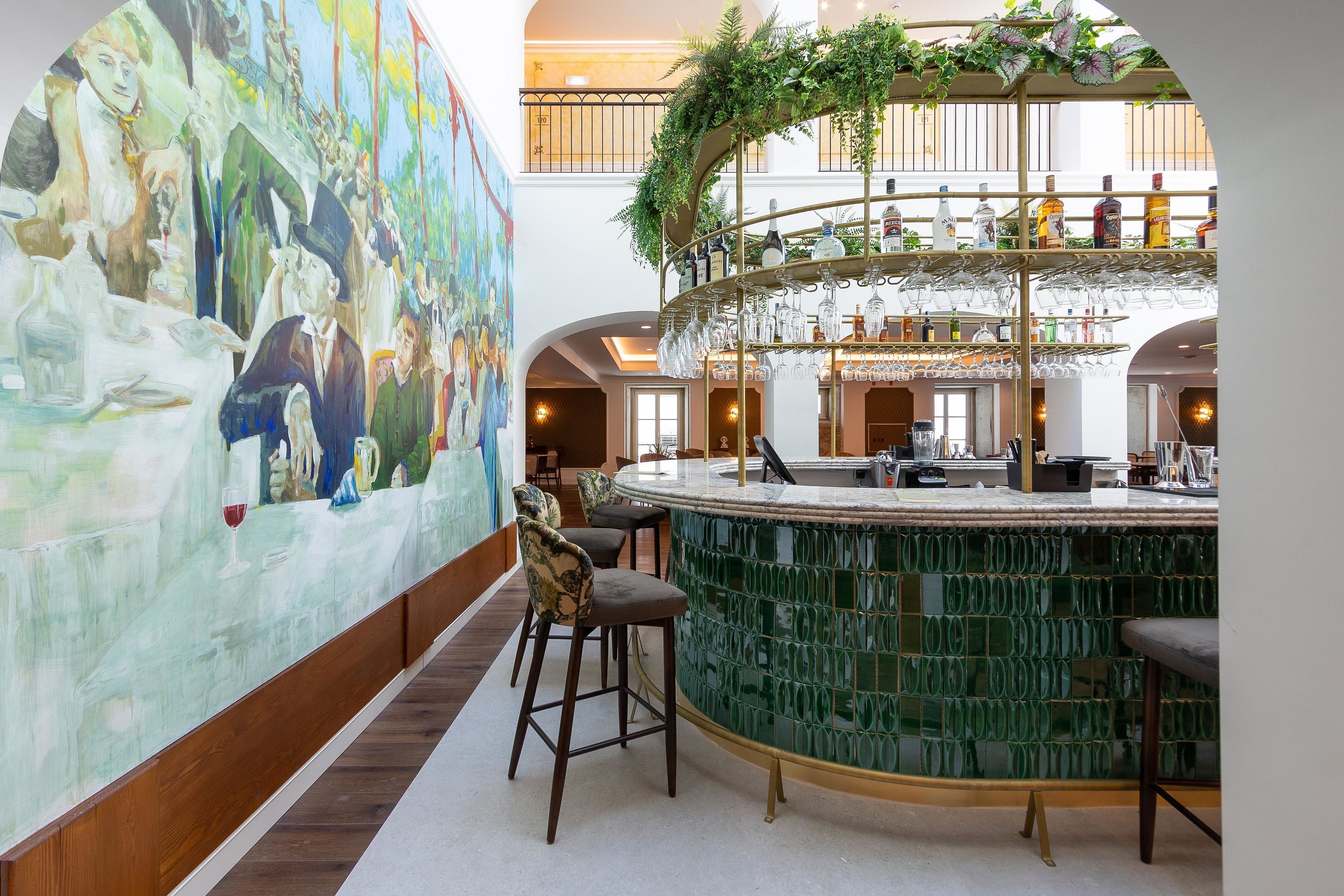 Uma área de bar com balcão em mosaico, banquetas e um mural na parede.