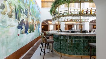 Uma área de bar com balcão em mosaico, banquetas e um mural na parede.