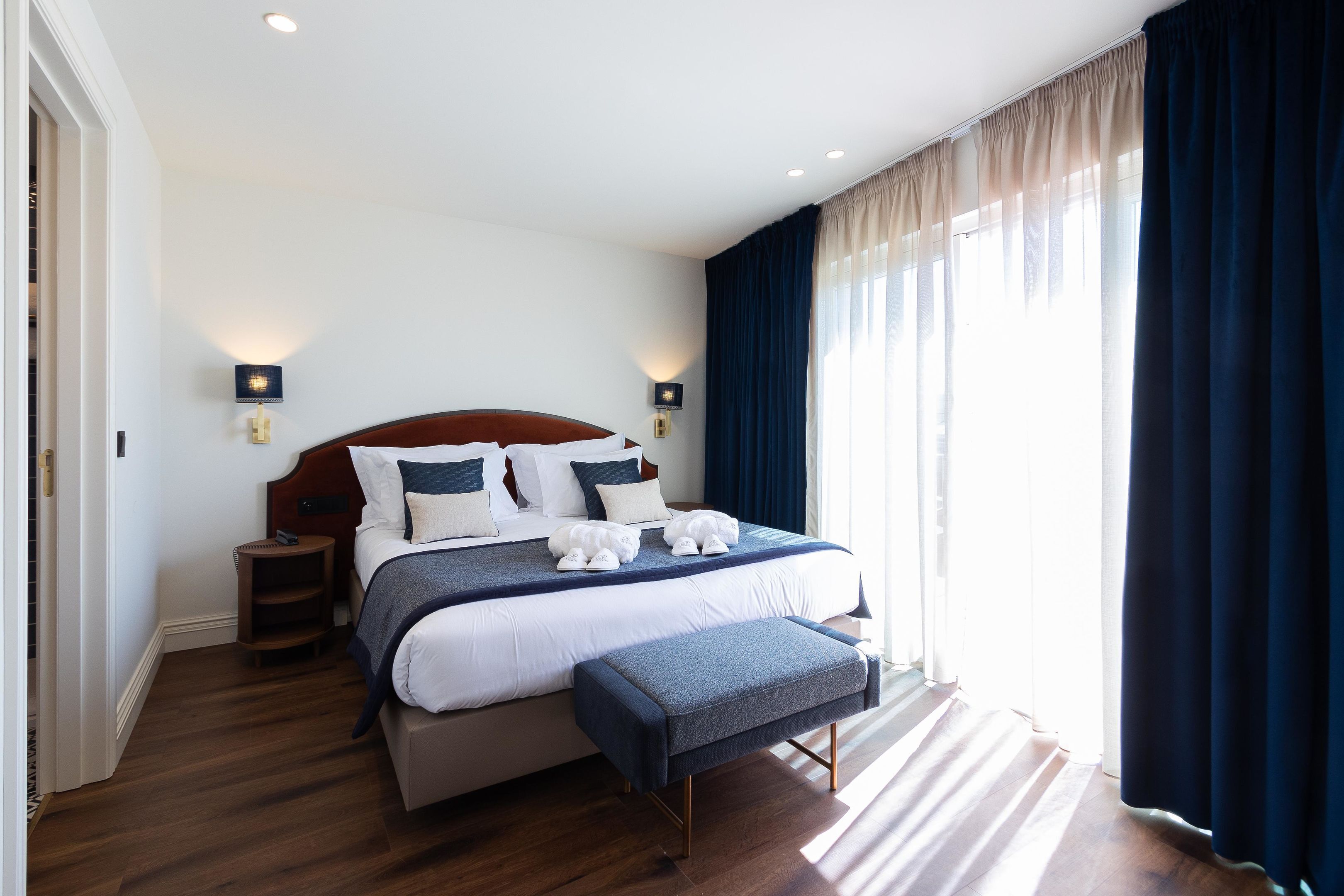 Quarto de hotel moderno com uma cama grande, mesas de cabeceira e vista para o exterior.